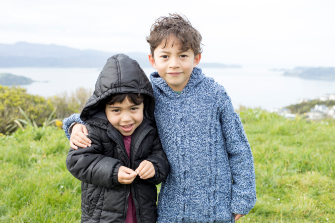 Two tamariki embracing, smiling and looking at the camera outdoors on a ...